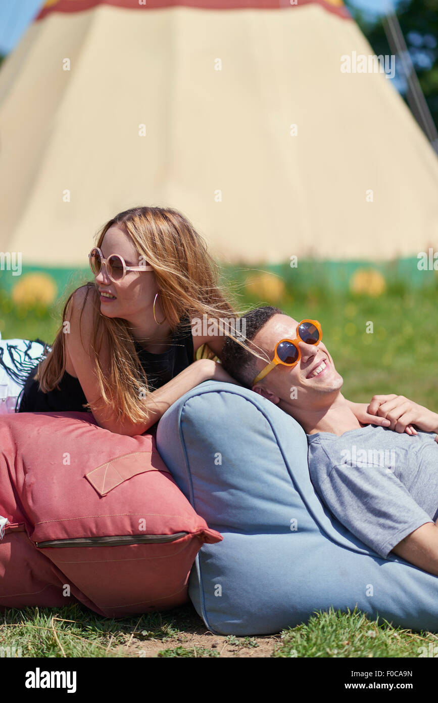 Happy couple lying on pillows while glamping, teepee in background ...
