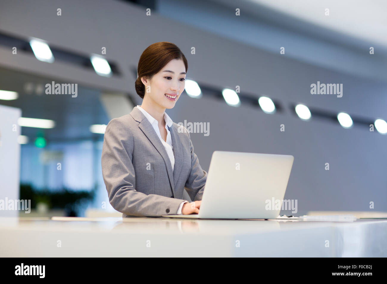 Confident receptionist using laptop at reception counter Stock Photo ...