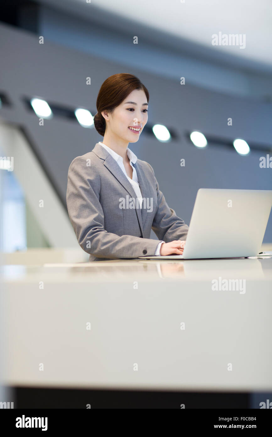 Confident receptionist using laptop at reception counter Stock Photo ...