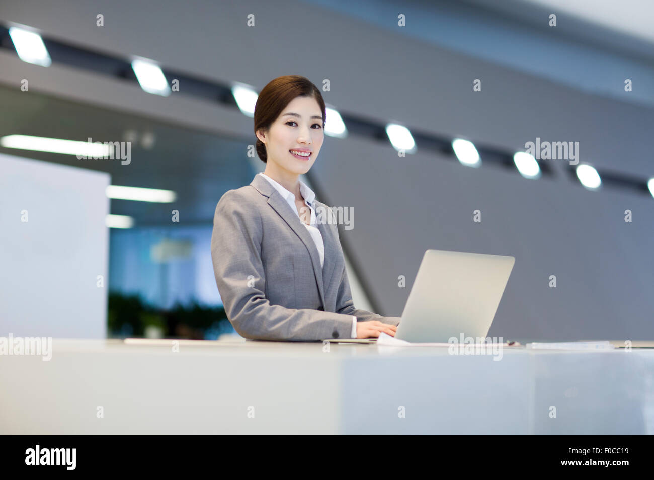 Confident receptionist using laptop at reception counter Stock Photo ...