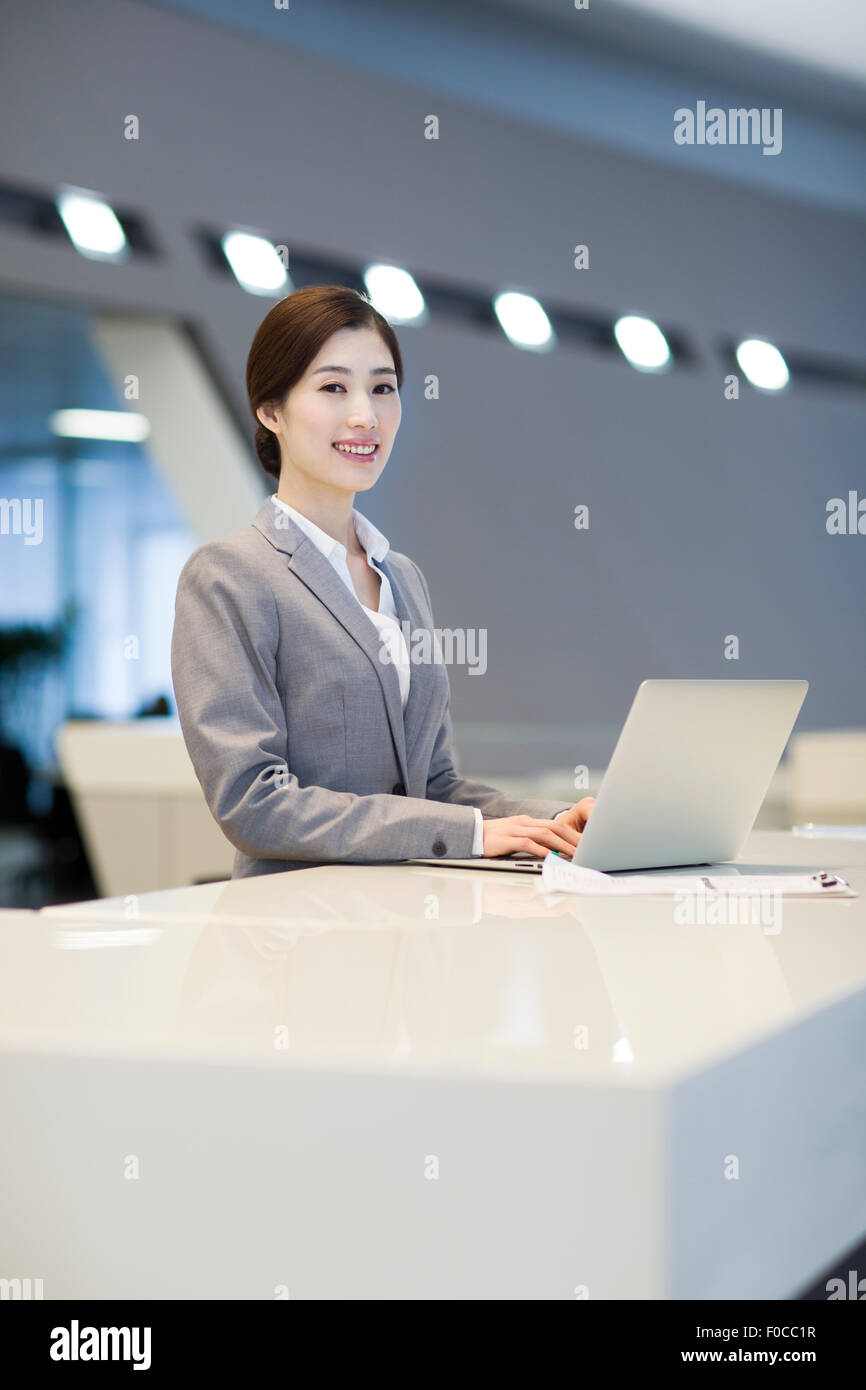Confident receptionist using laptop at reception counter Stock Photo ...