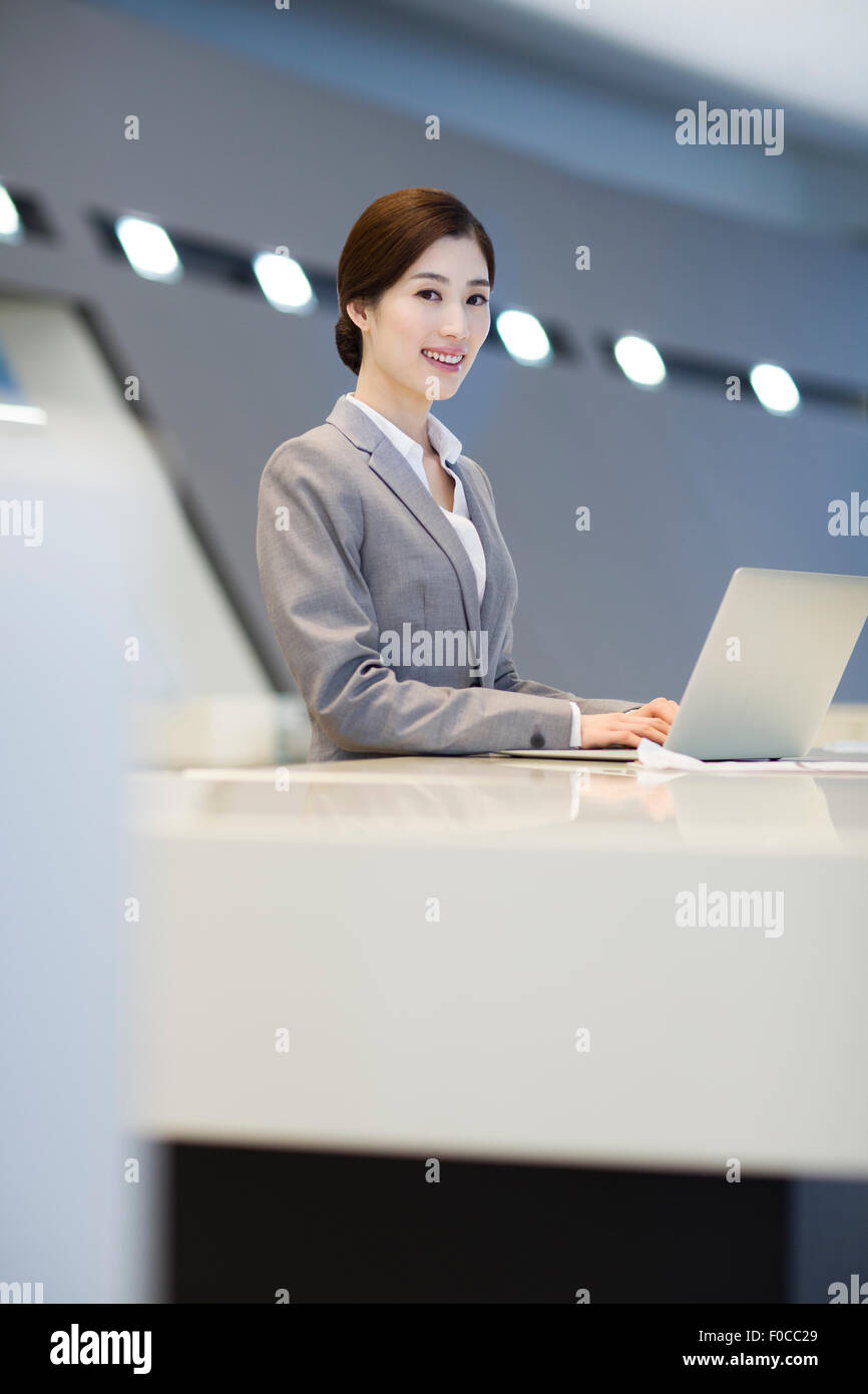 Confident receptionist using laptop at reception counter Stock Photo ...