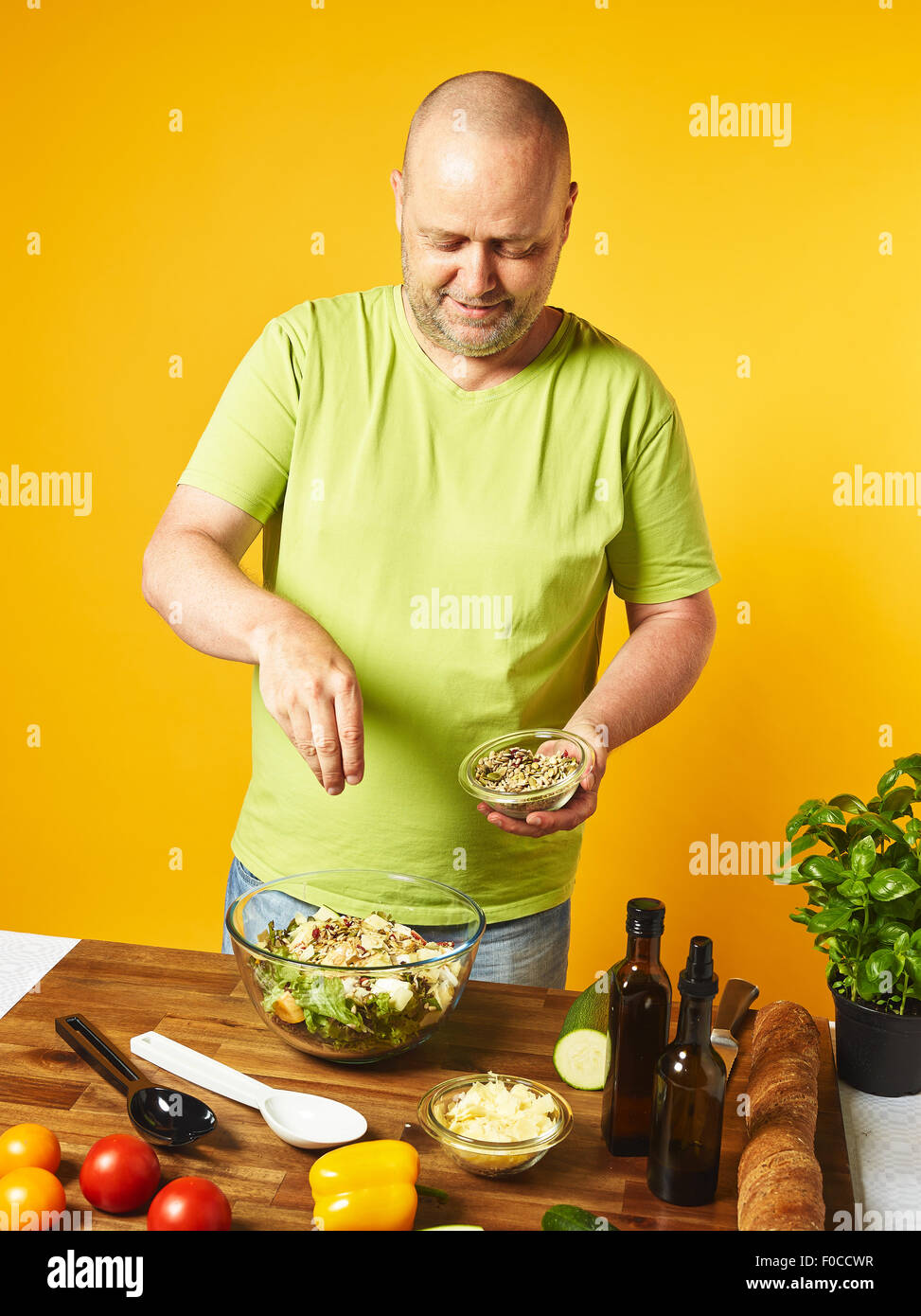 Fresh salad ingredients on the table, middle-aged man sprinkle seeds ...