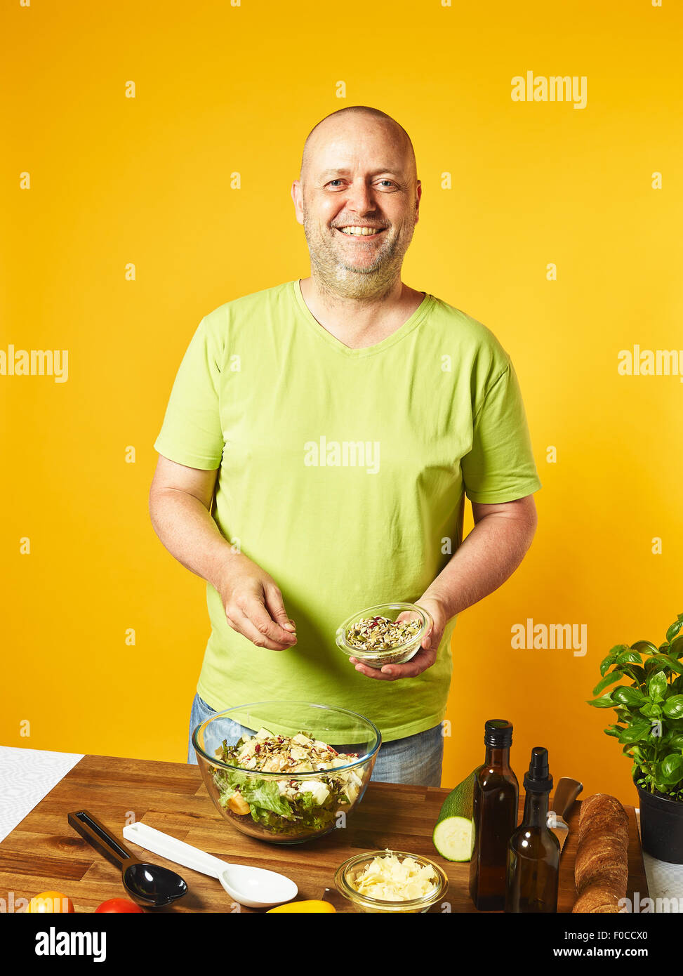 Fresh salad ingredients on the table, middle-aged man sprinkle seeds ...