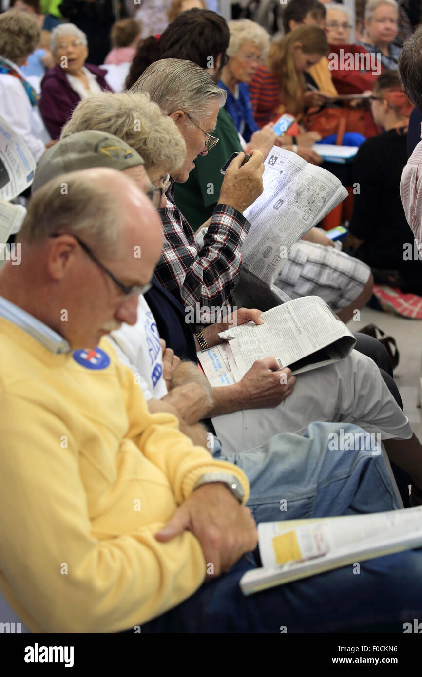 People sitting in audience on rows of chairs reading while waiting for ...