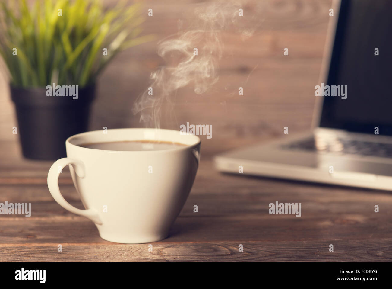 Morning caffeine concept. Wooden business desk with laptop, cup of hot ...