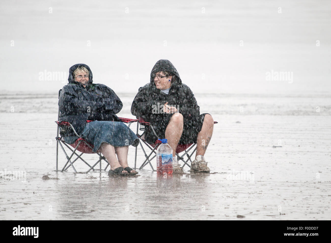 Two people sitting on a beach in a heavy rainstorm. Both are laughing ...