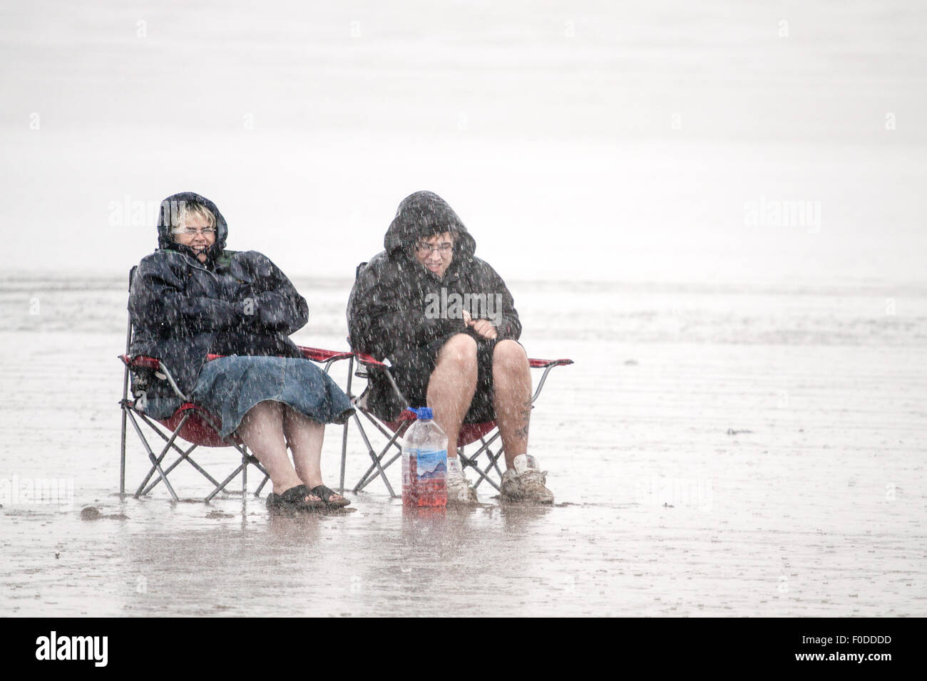 Two people sitting on a beach in a rainstorm Stock Photo - Alamy