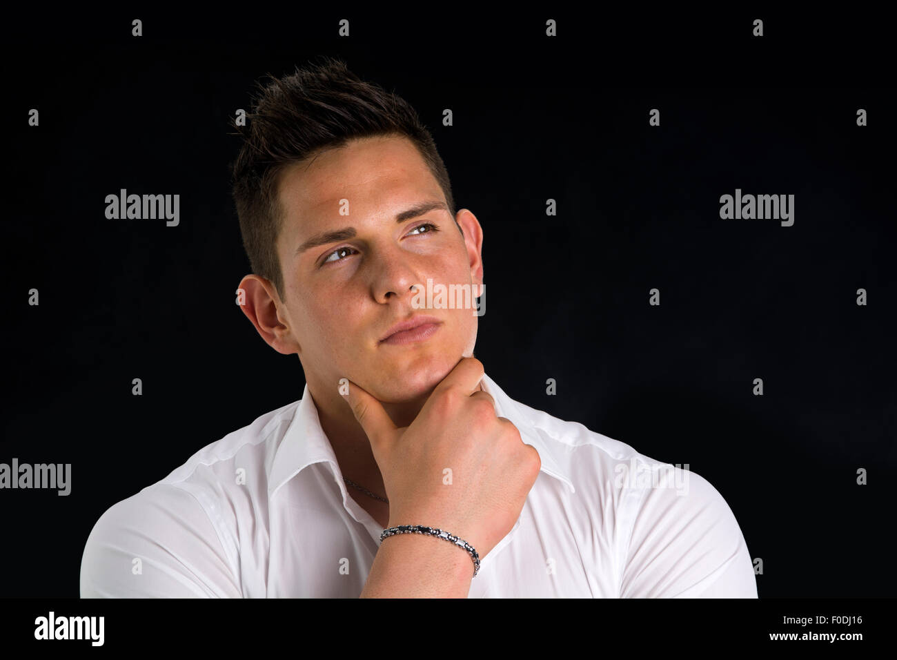 Attractive young man thinking, looking up with hand on his chin ...