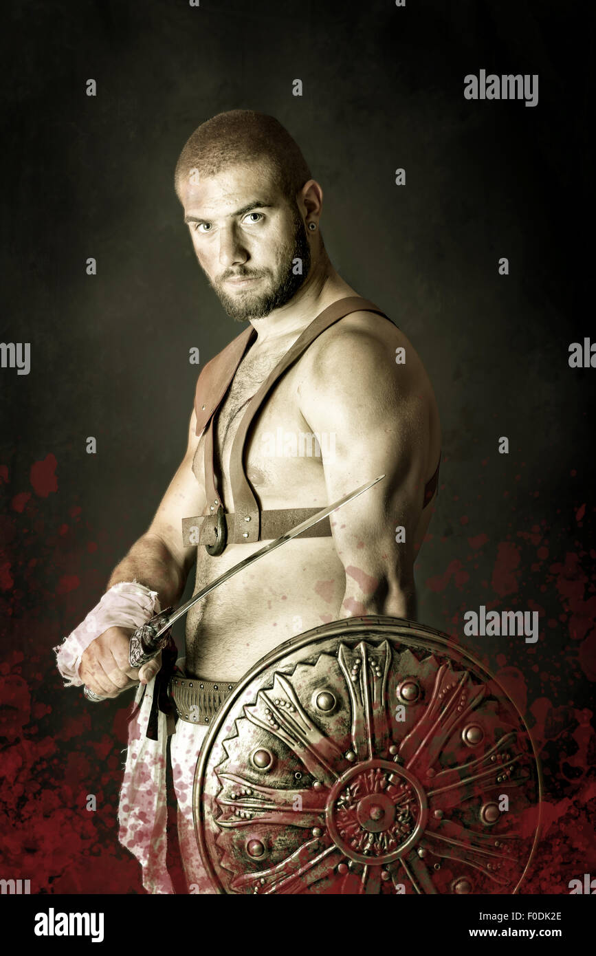 Gladiator posing with shield and sword in a dark background with blood ...