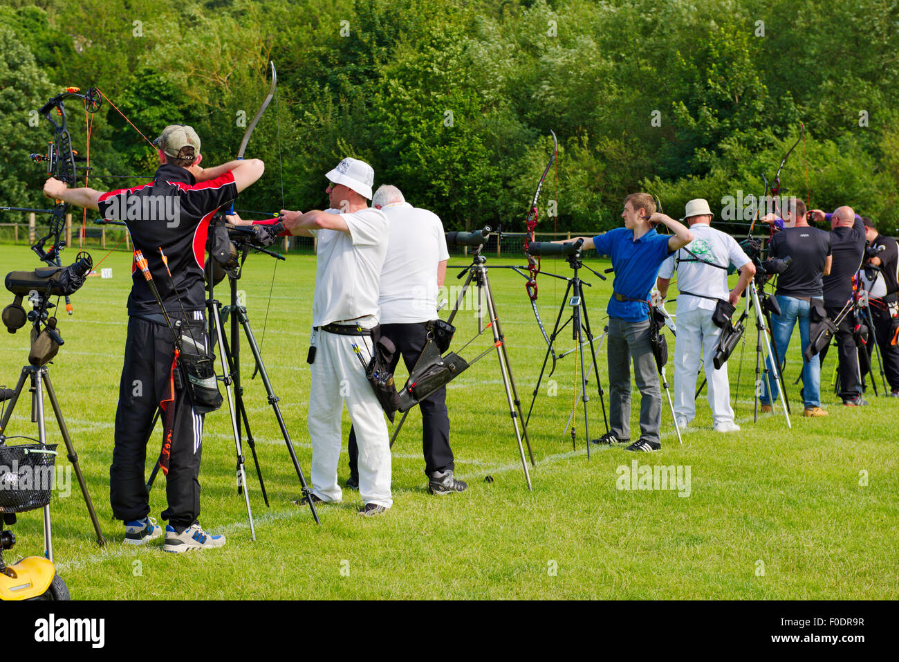 Row of male archers in line shooting various style bows in competition ...