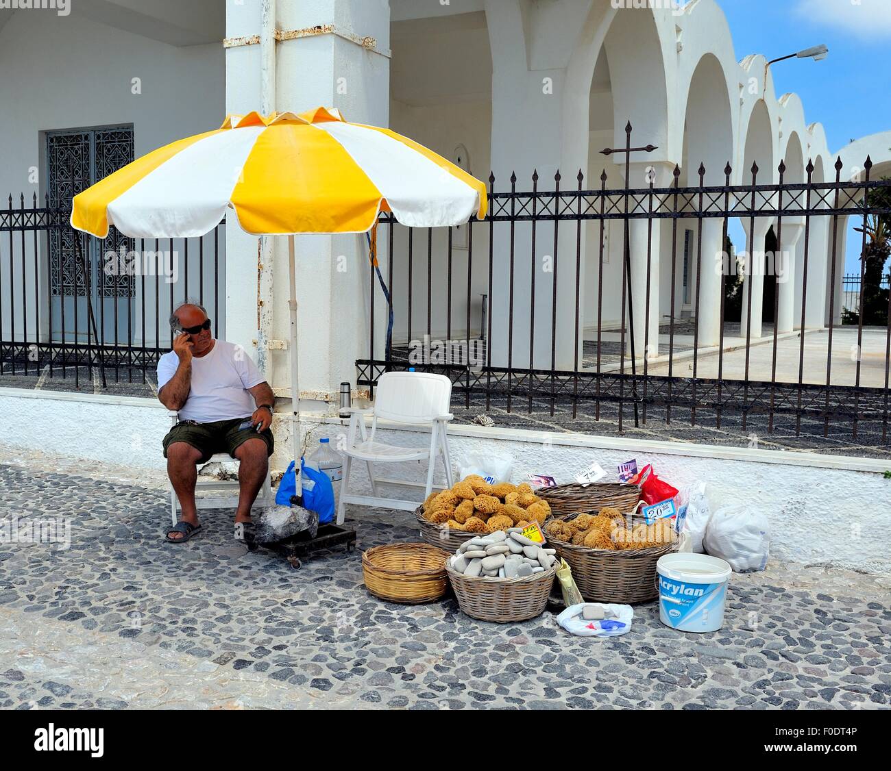 A man sitting under a white and yellow parasol selling Sponges and ...