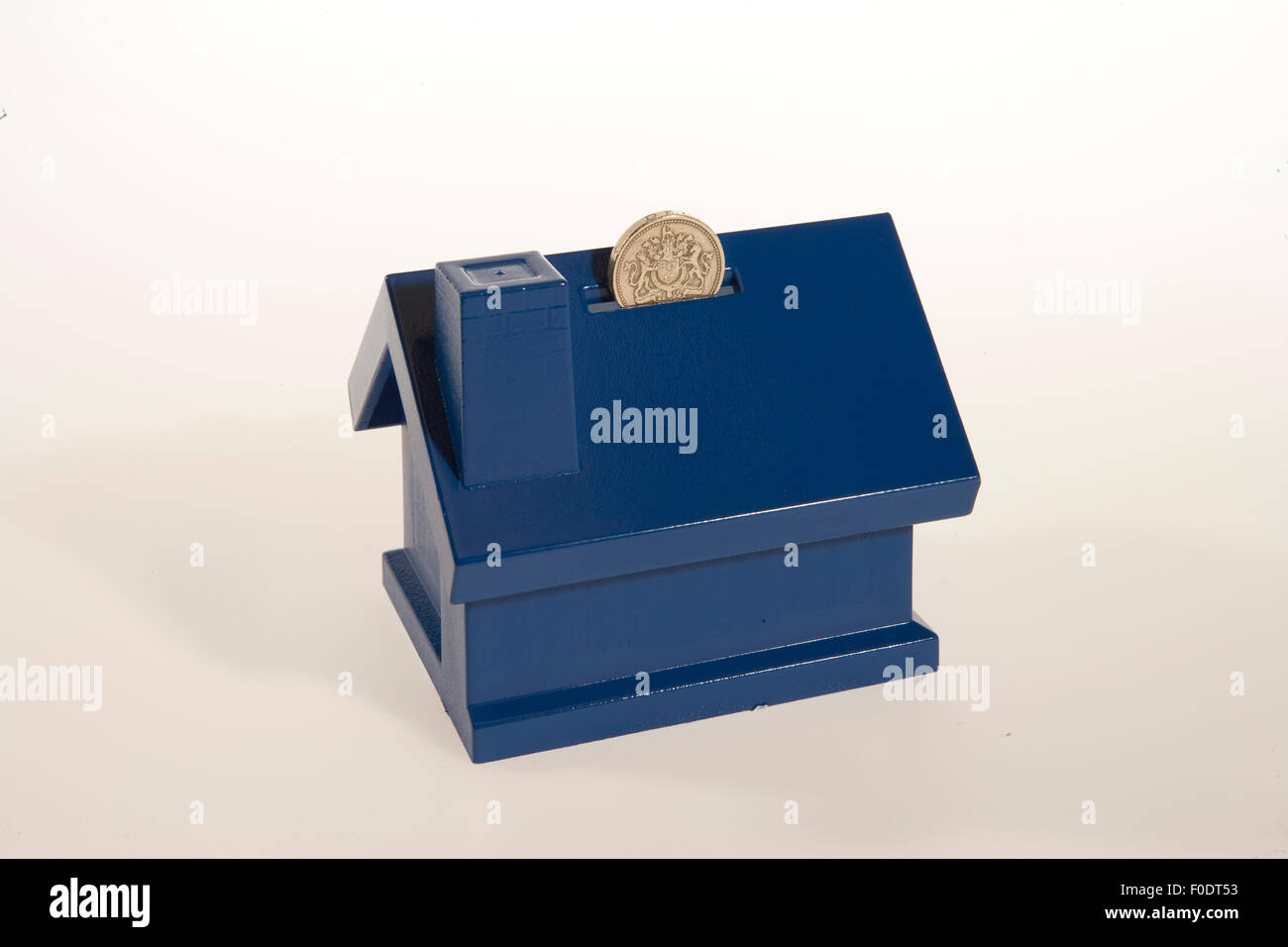 Blue coloured house shaped money box with UK sterling pound coin being ...