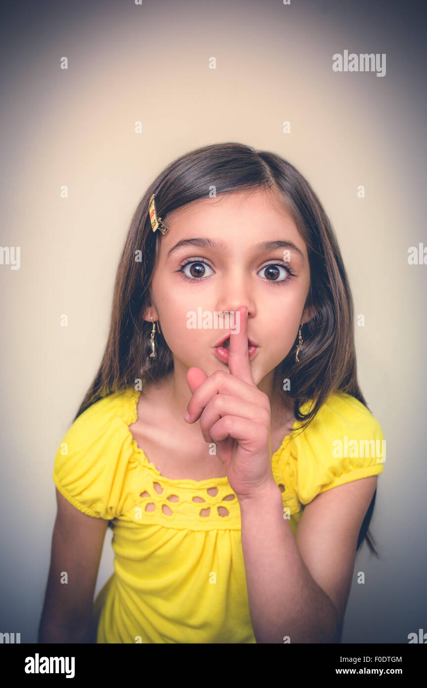 Young girl with finger to lips hushing at the camera Stock Photo - Alamy