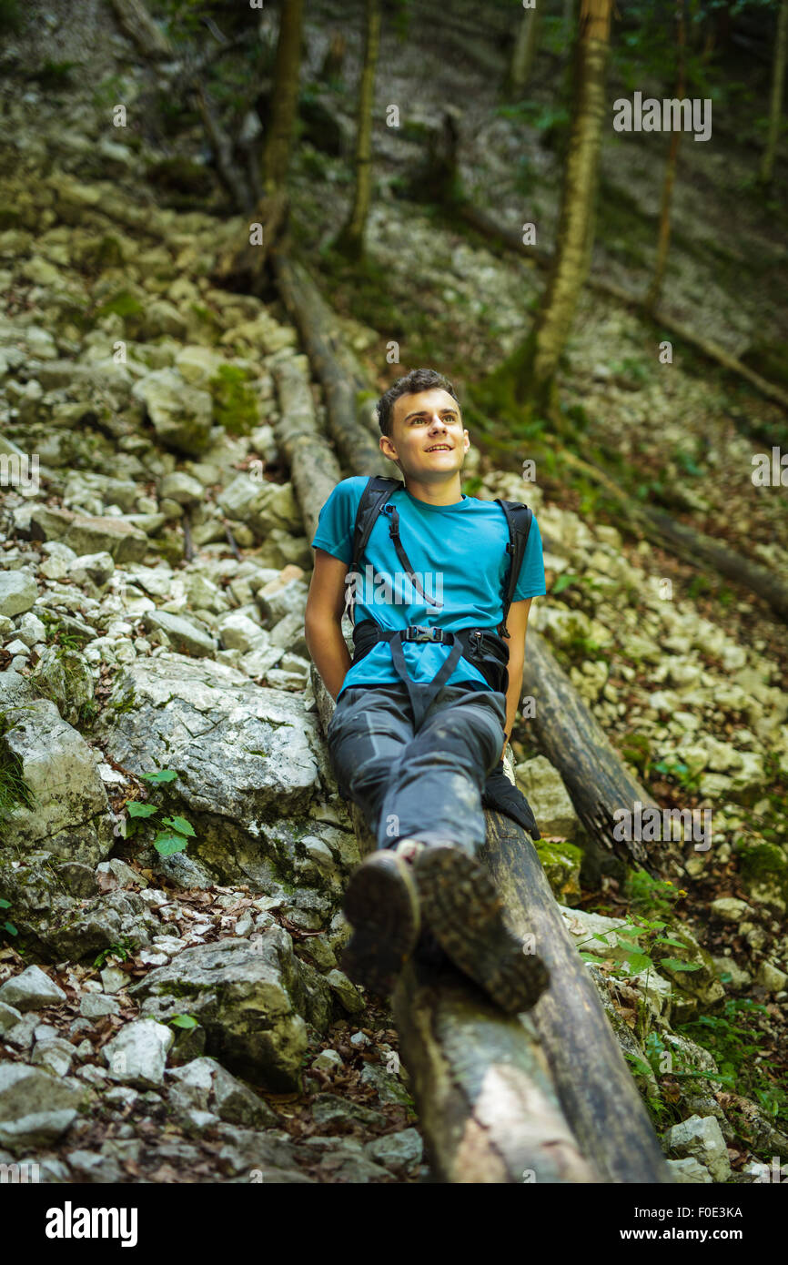 Happy teenager sitting on a log, resting after hiking on a forest trail ...