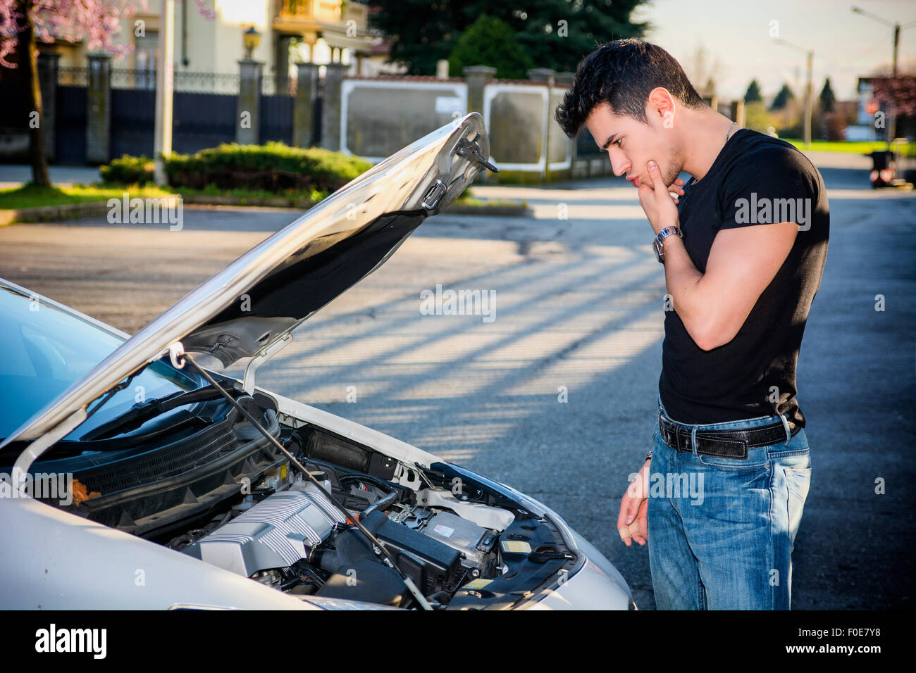 Handsome young man trying to repair a car engine, looking inside open ...