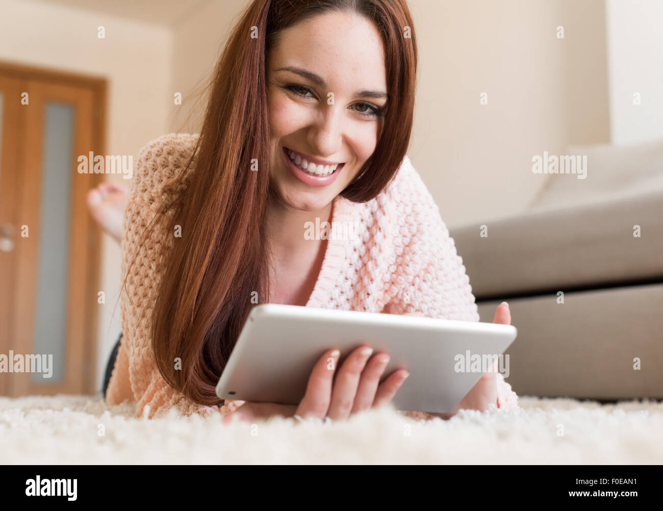 Woman laying down on carpet with a tablet Stock Photo - Alamy