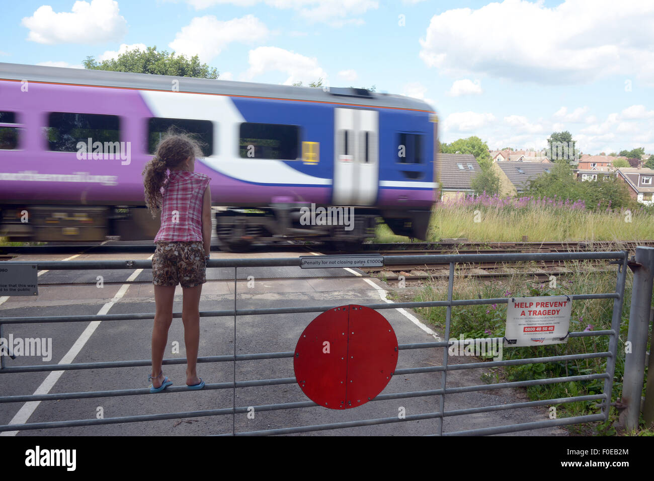 A young girl climbs on a gate at a level crossing to watch the trains ...