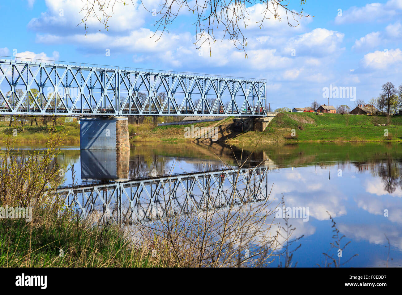 Side view of blue steel bridge on a river with reflection of cloudy ...