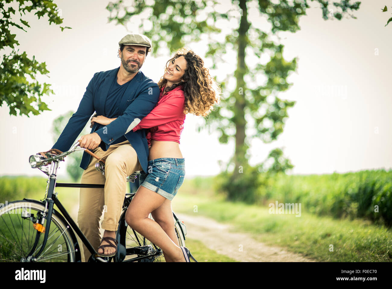 Happy couple having fun while biking on a country road Stock Photo - Alamy