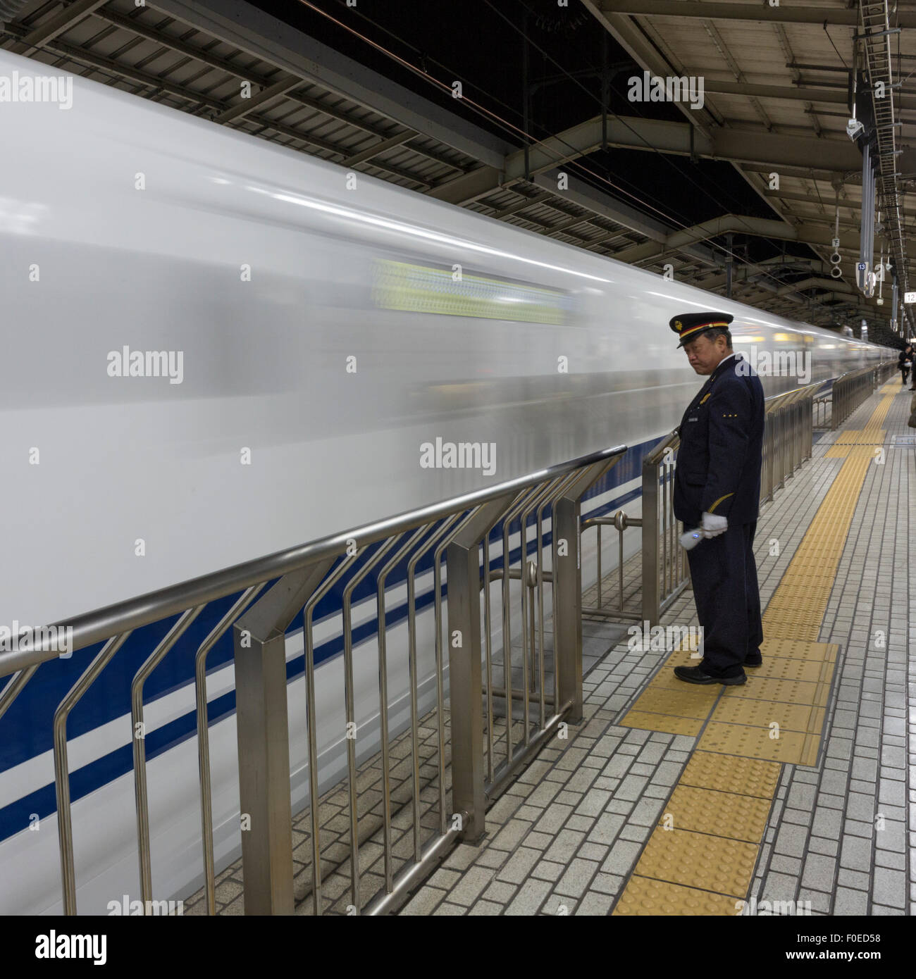 Station agent watching a bullet train (shinkansen) depart in a blur of ...