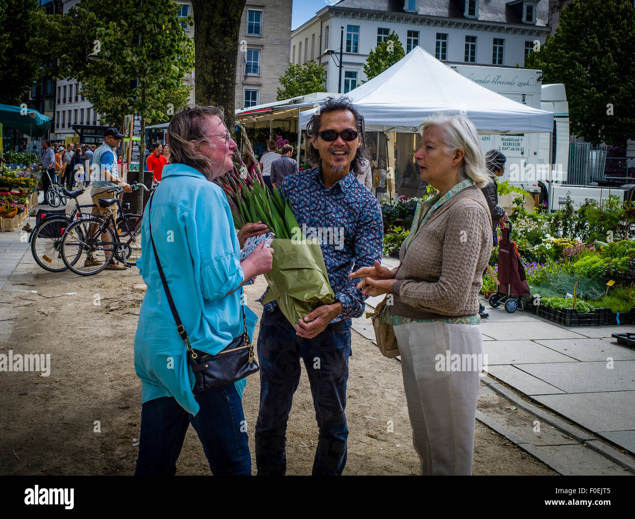 Two women talk to a man holding gladiolas in the flower market at the ...