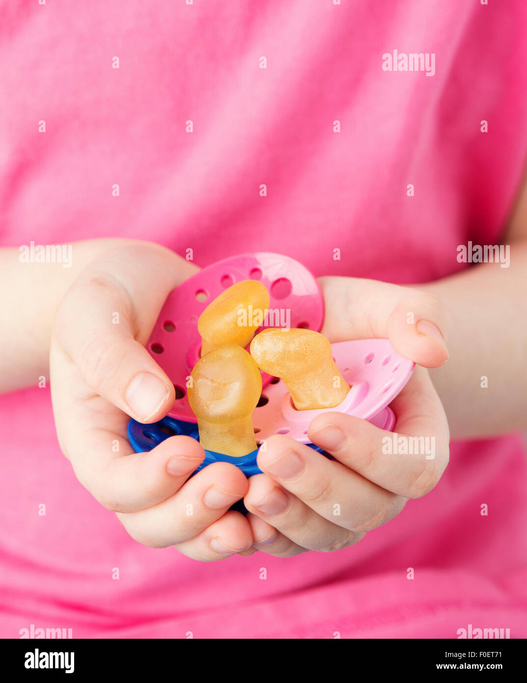 Close up of child hands holding three pacifiers. Little girl showing ...