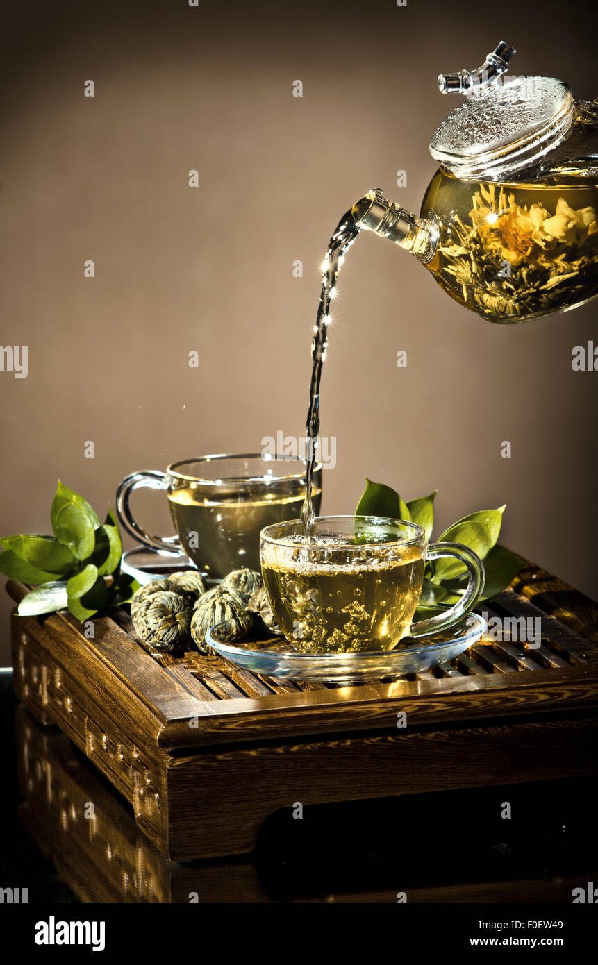 vertical photo, of the glass teapot flow green tea in cup on brown ...
