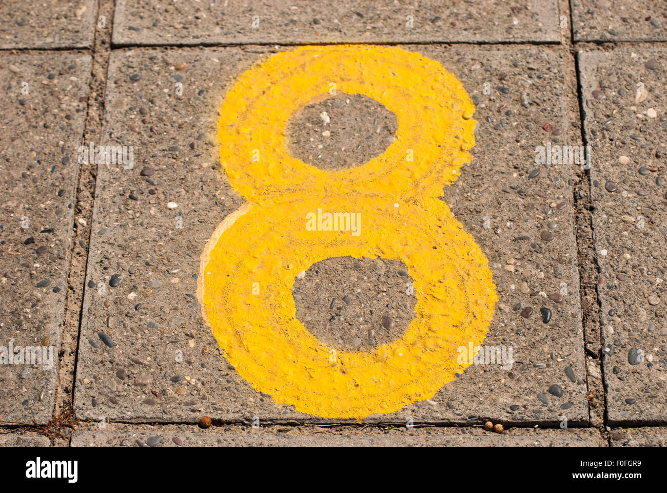 number eight painted bright yellow paint on a gray tile of pathway ...