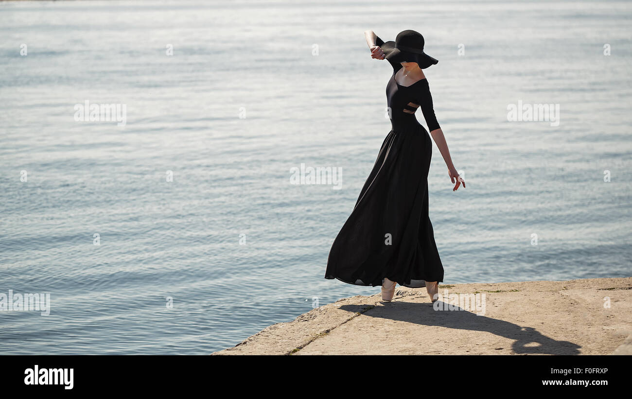 Young slender dancer in a hat and a long black dress dancing on the ...