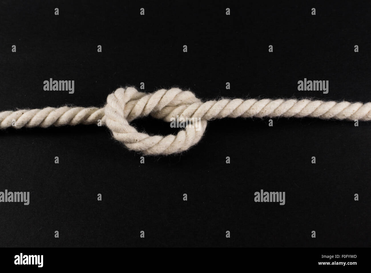 Single knot tied in a length of white rope against a black studio ...