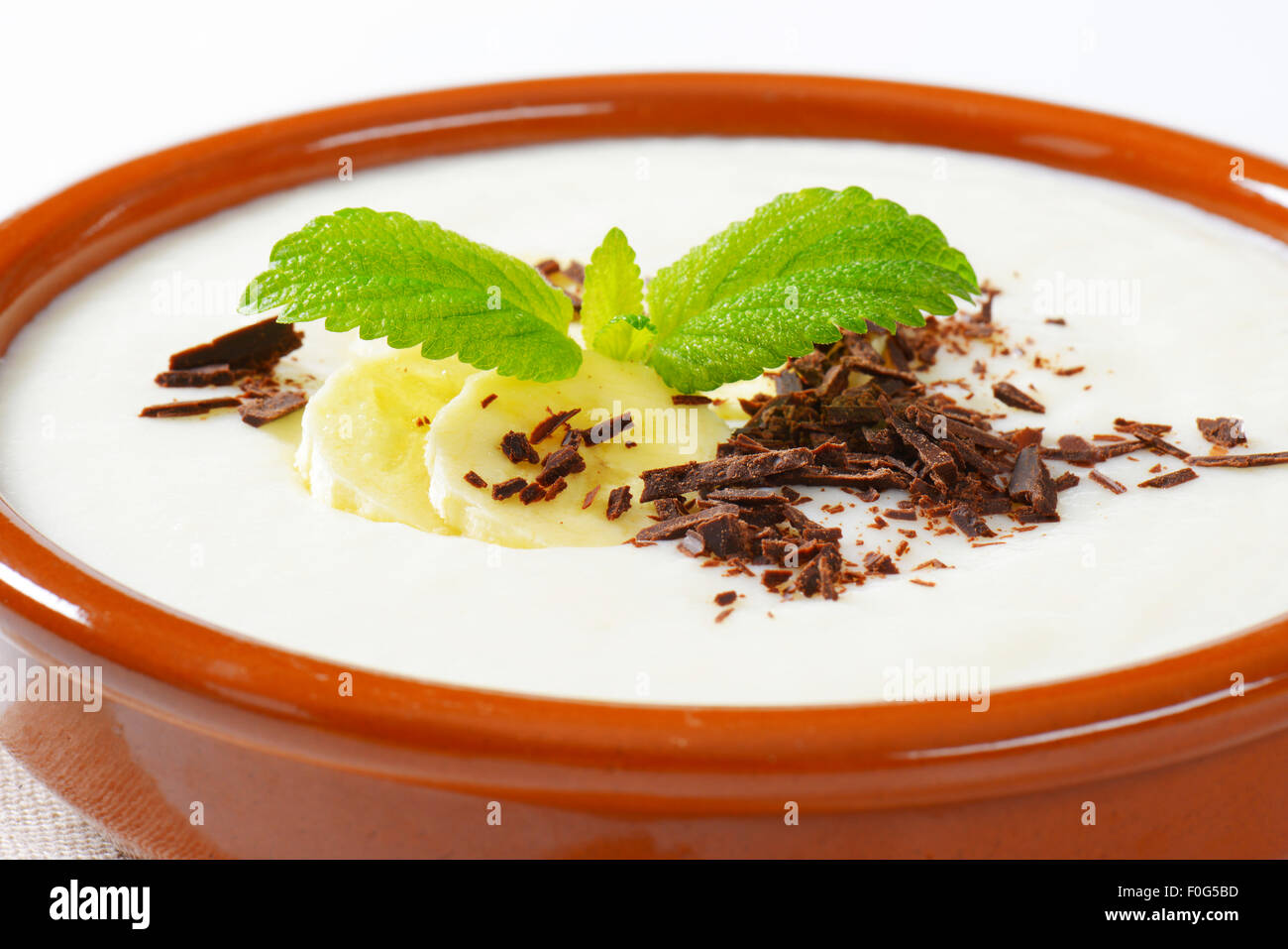 Bowl of smooth milk pudding with sliced banana and grated chocolate ...