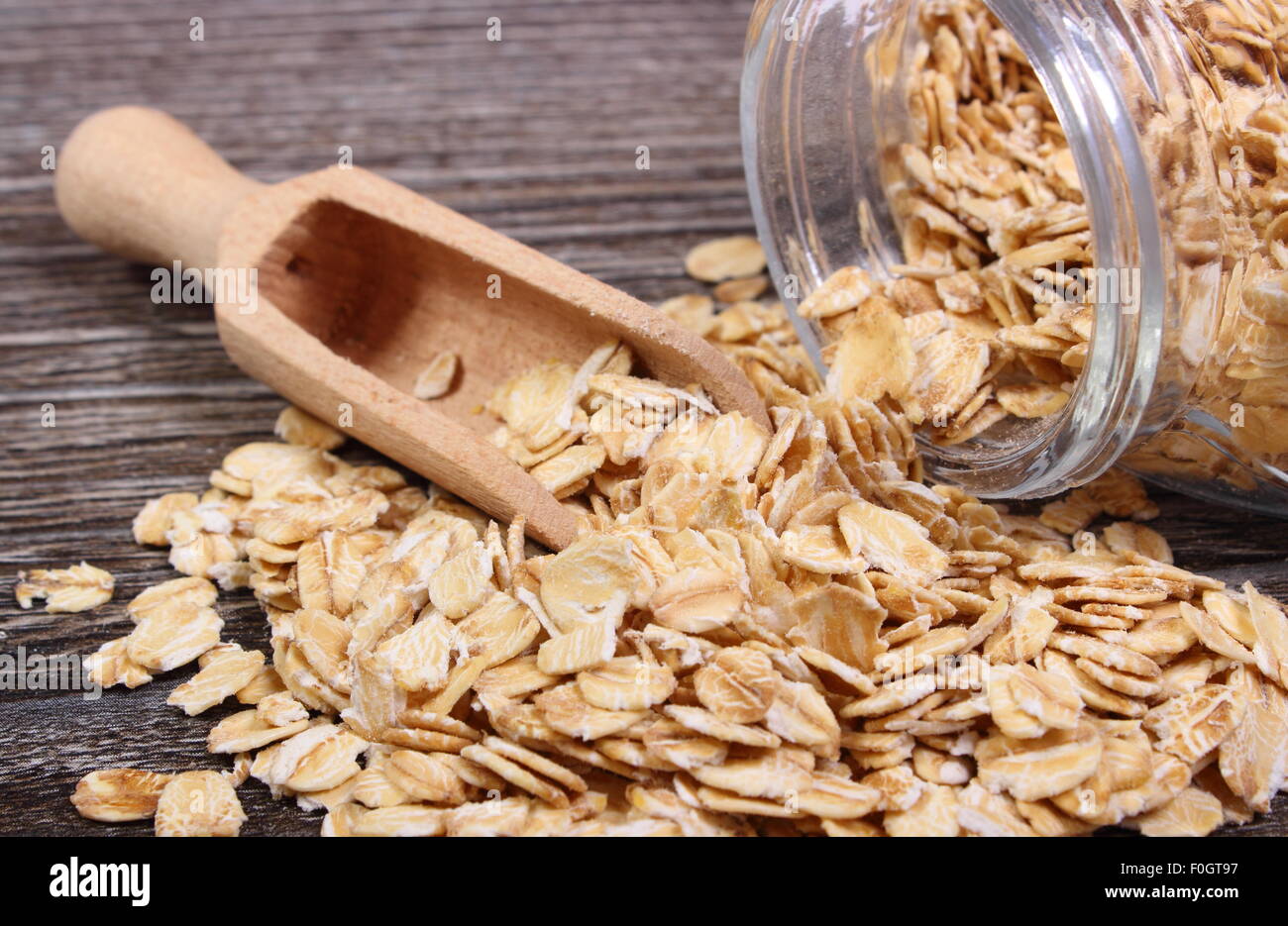 Heap of organic oatmeal, oat flakes spilling out of glass jar on wooden ...