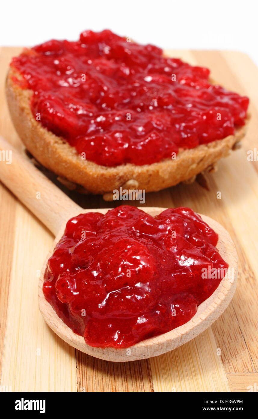 Homemade strawberry jam on wooden spoon and portion of whole wheat ...