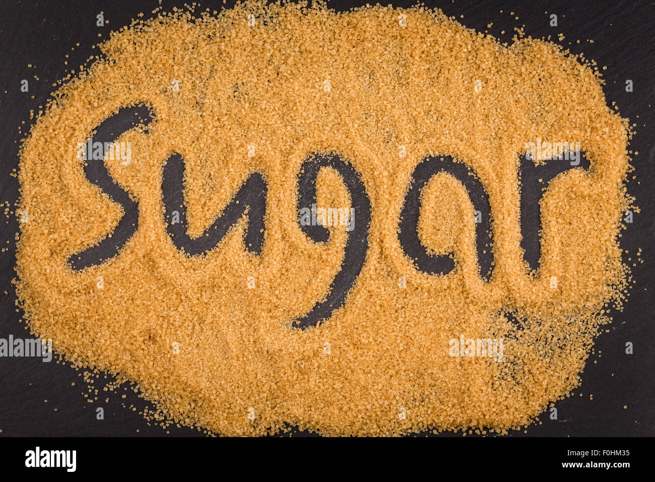 word sugar written in brown granulated sugar on dark stone background ...