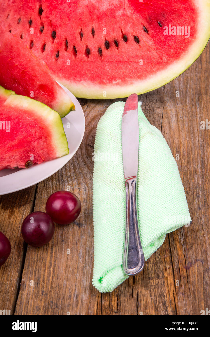 slices of watermelon on the plate next with plums on a wooden ...