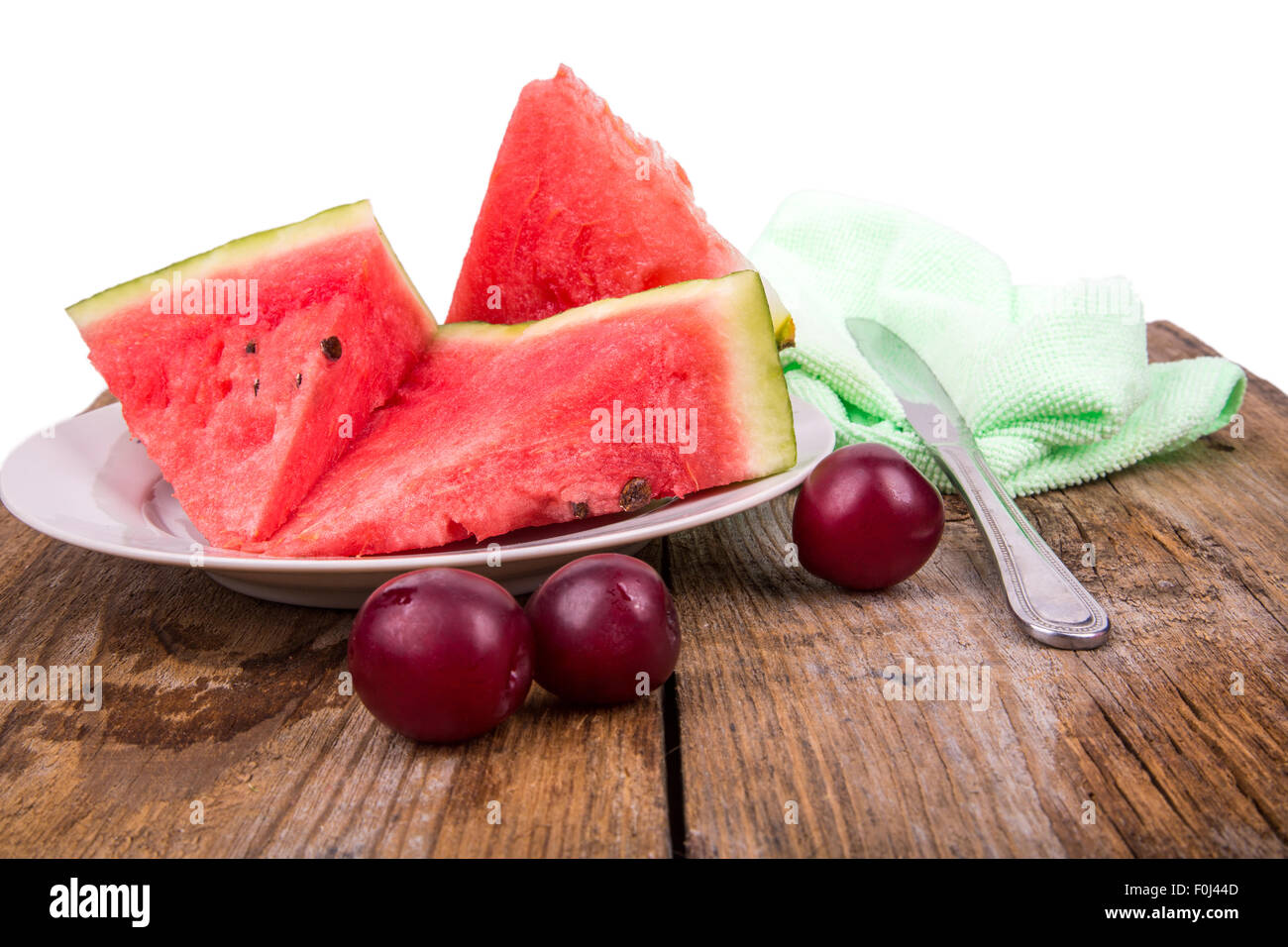 slices of watermelon on the plate next with plums on a wooden ...