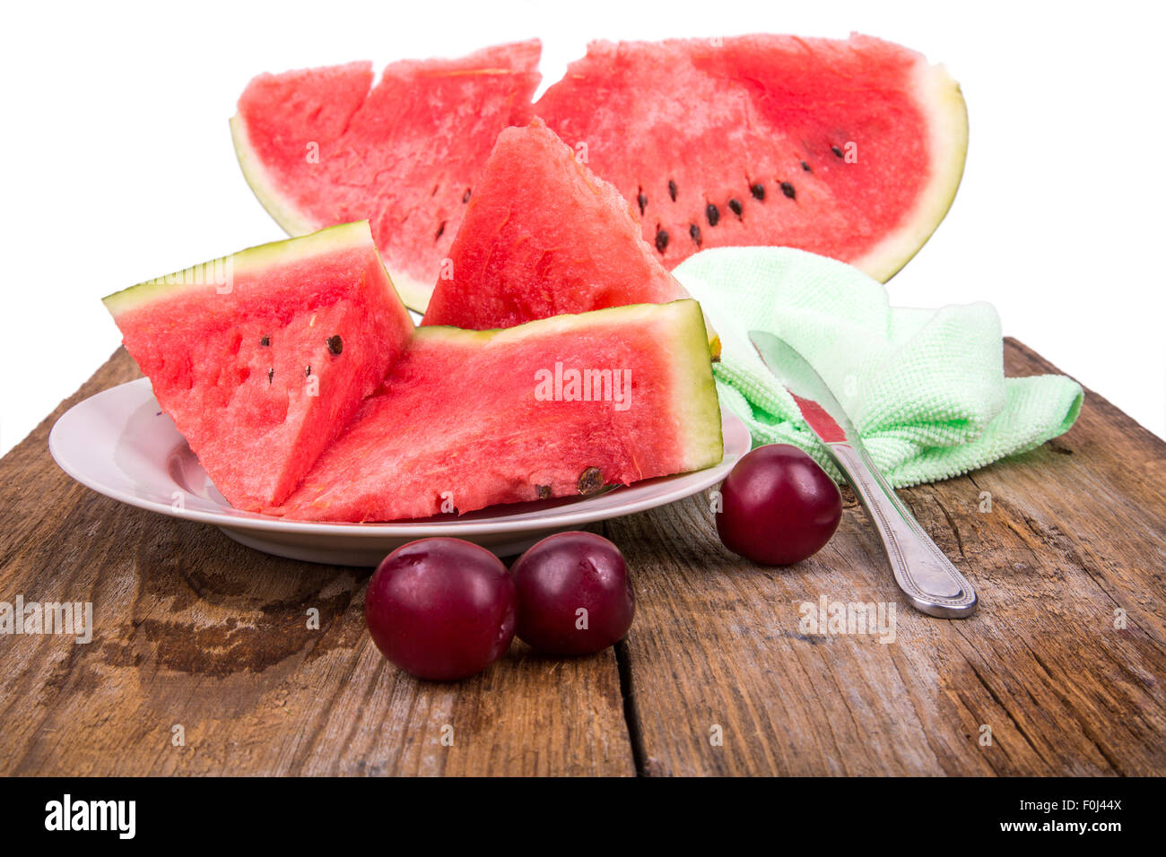 slices of watermelon on the plate next with plums on a wooden ...