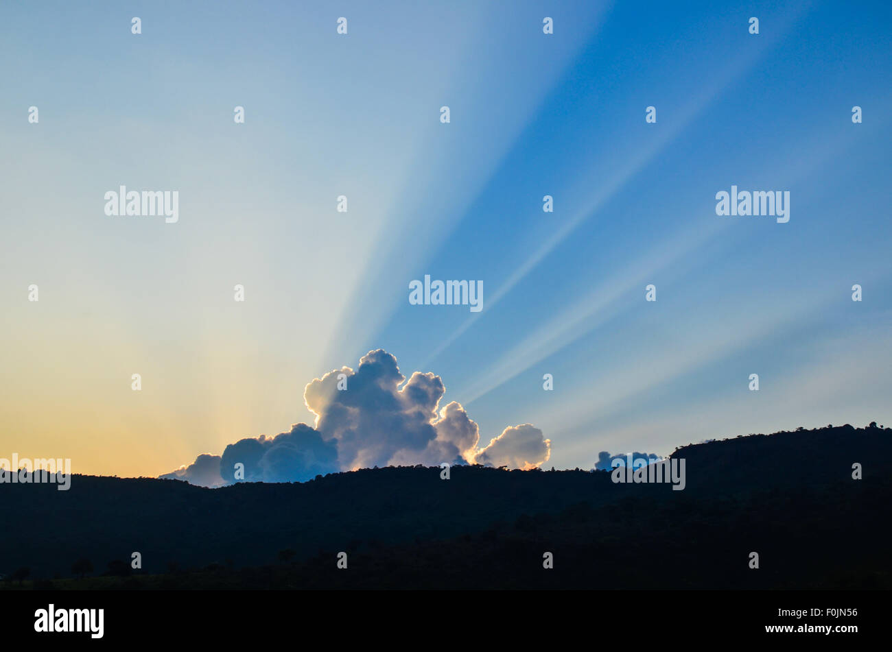 Geometric sun rays behind clouds in the blue sky, in the shape of a ...
