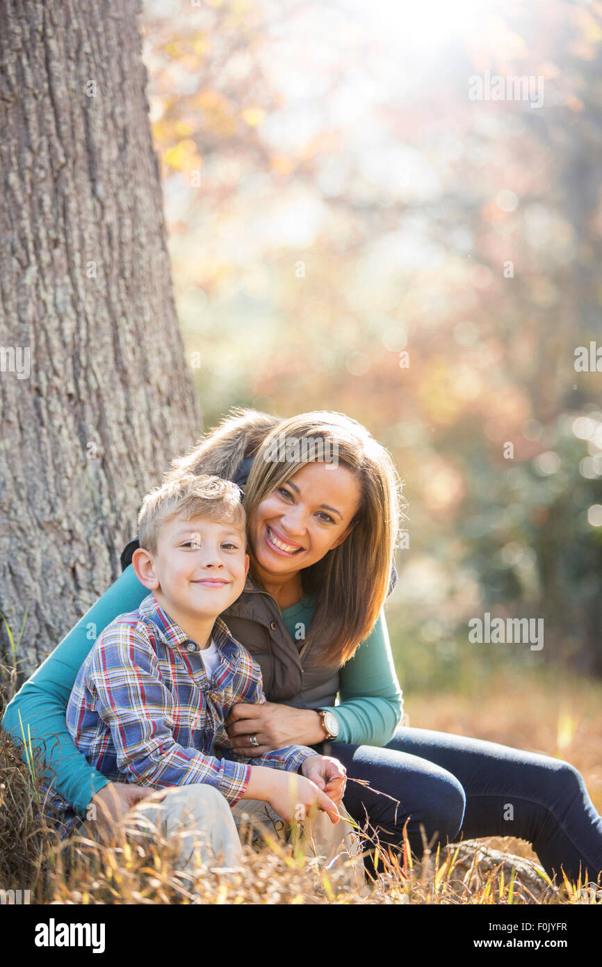 Portrait smiling mother and son at tree trunk in autumn woods Stock ...