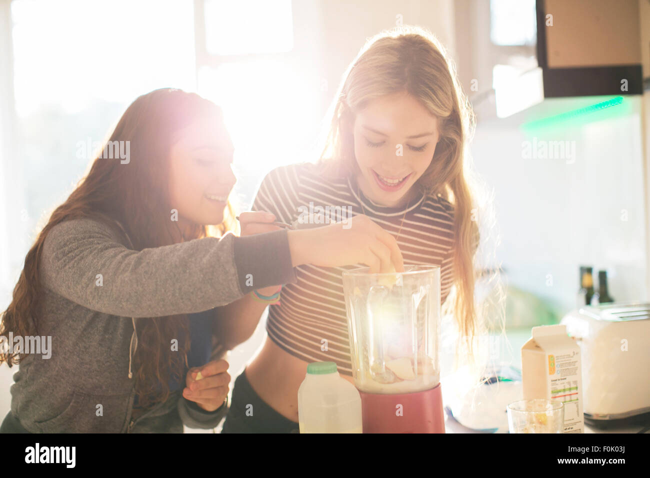 Teenage girls making smoothie in sunny kitchen Stock Photo - Alamy