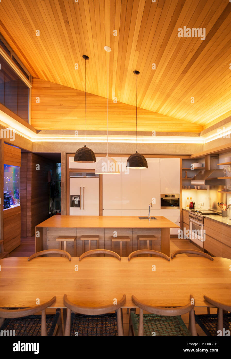 Illuminated slanted wood ceiling over luxury kitchen and dining table ...