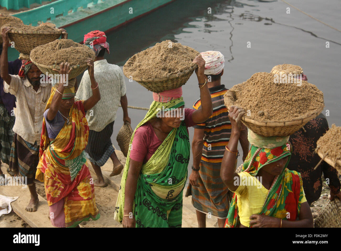 Male and female laborers carry heavy loads of sand balanced on their ...