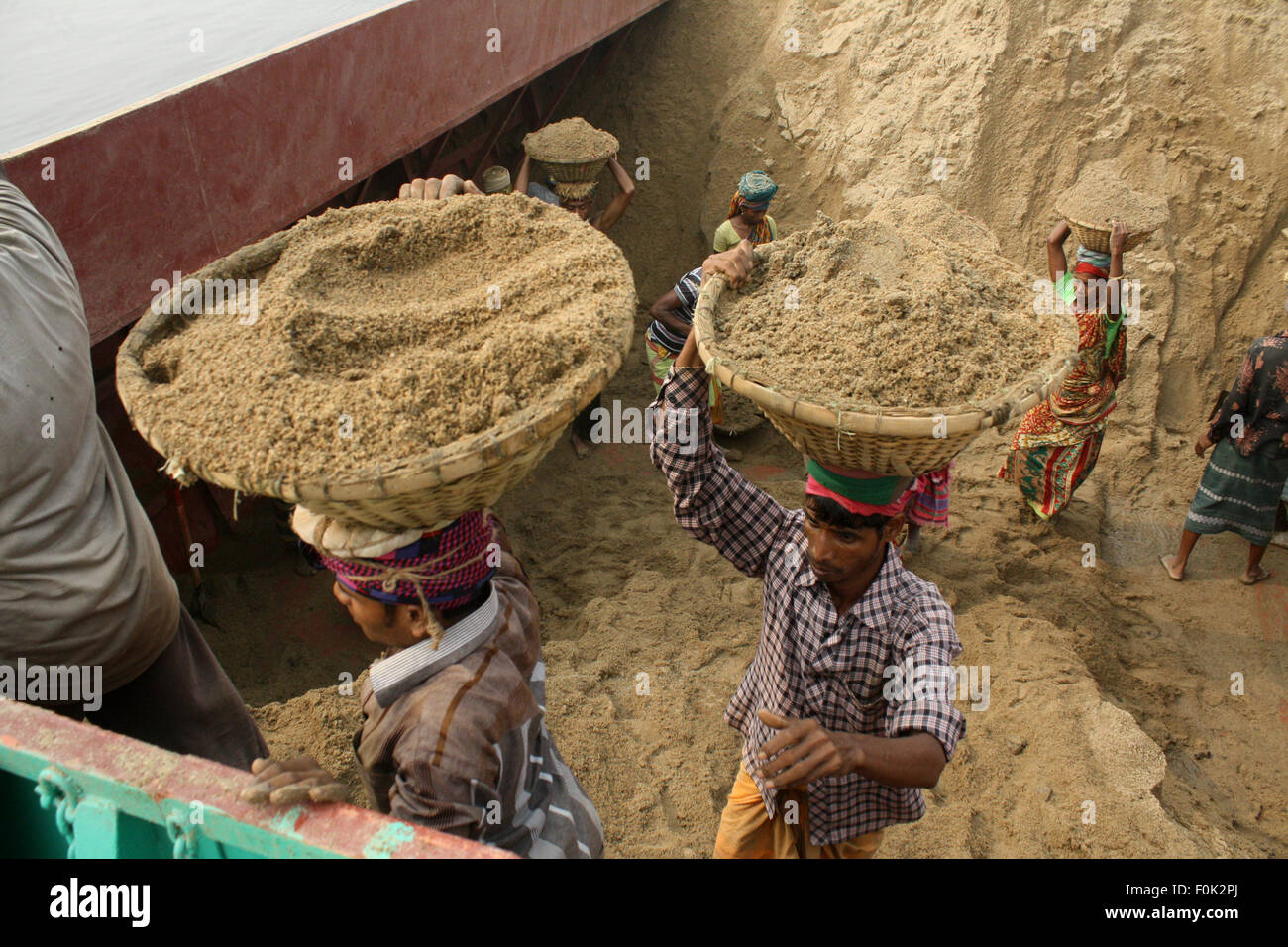 Male and female laborers carry heavy loads of sand balanced on their ...