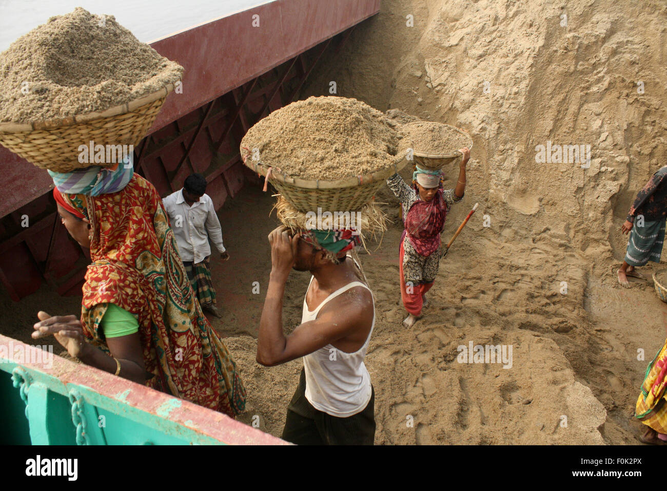 Male and female laborers carry heavy loads of sand balanced on their ...
