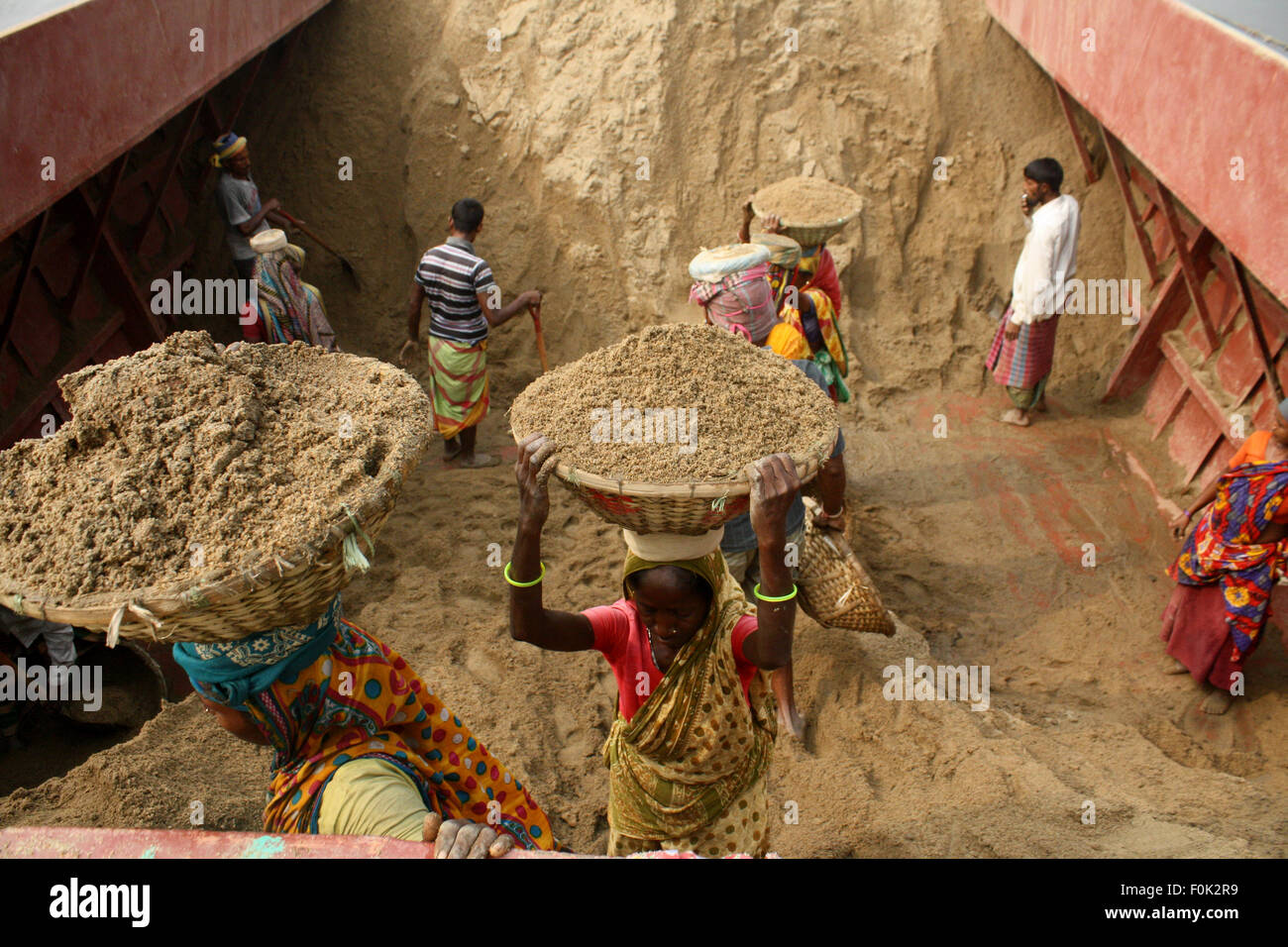 Male and female laborers carry heavy loads of sand balanced on their ...