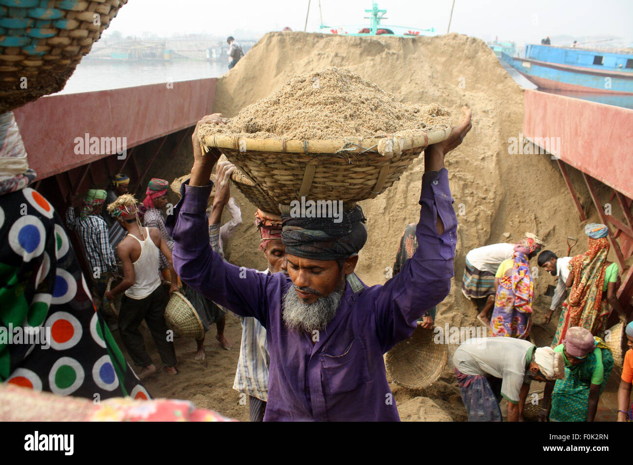 Male and female laborers carry heavy loads of sand balanced on their ...