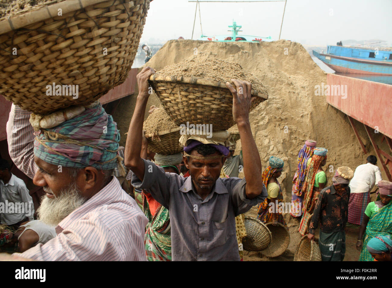 Male and female laborers carry heavy loads of sand balanced on their ...