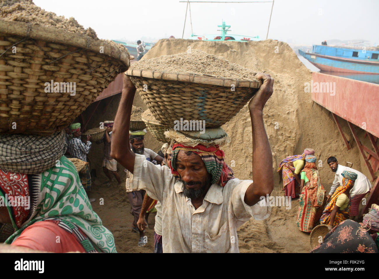 Male and female laborers carry heavy loads of sand balanced on their ...