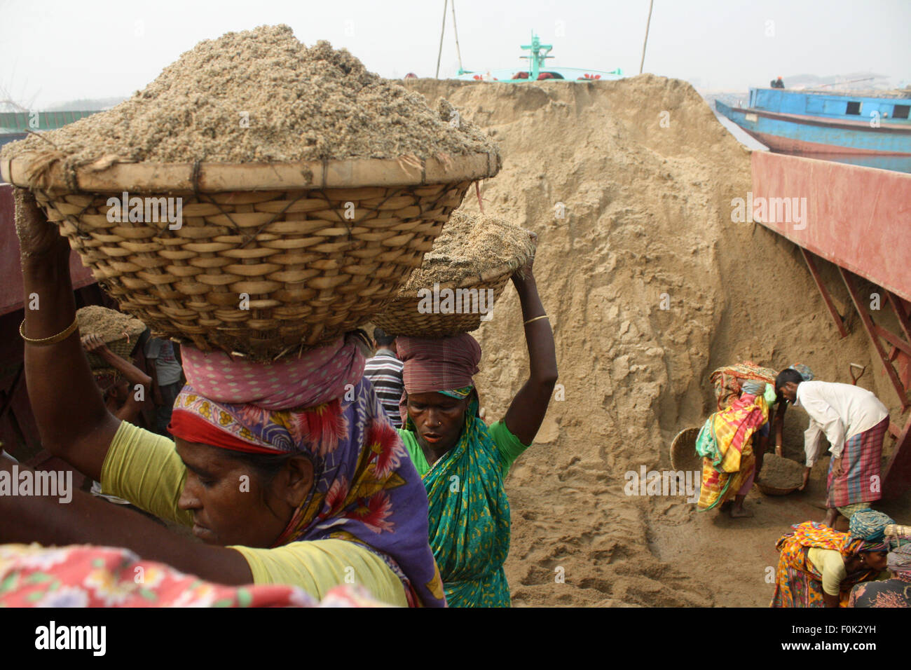 Male and female laborers carry heavy loads of sand balanced on their ...